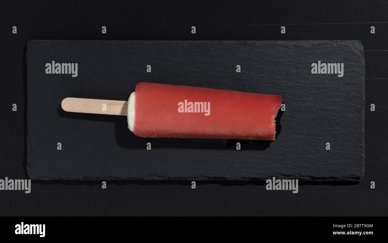 Top view of Red ice cream stick on natural stone black plate background ...