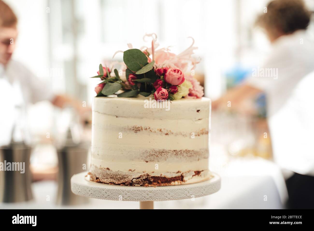 Close up sweet small round white cake on stand. Pink flower decoration ...