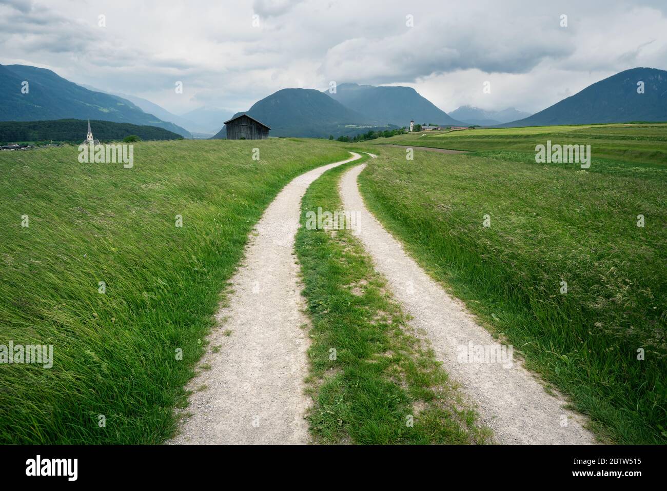 Winding path through grass meadows to villages with churches with ...