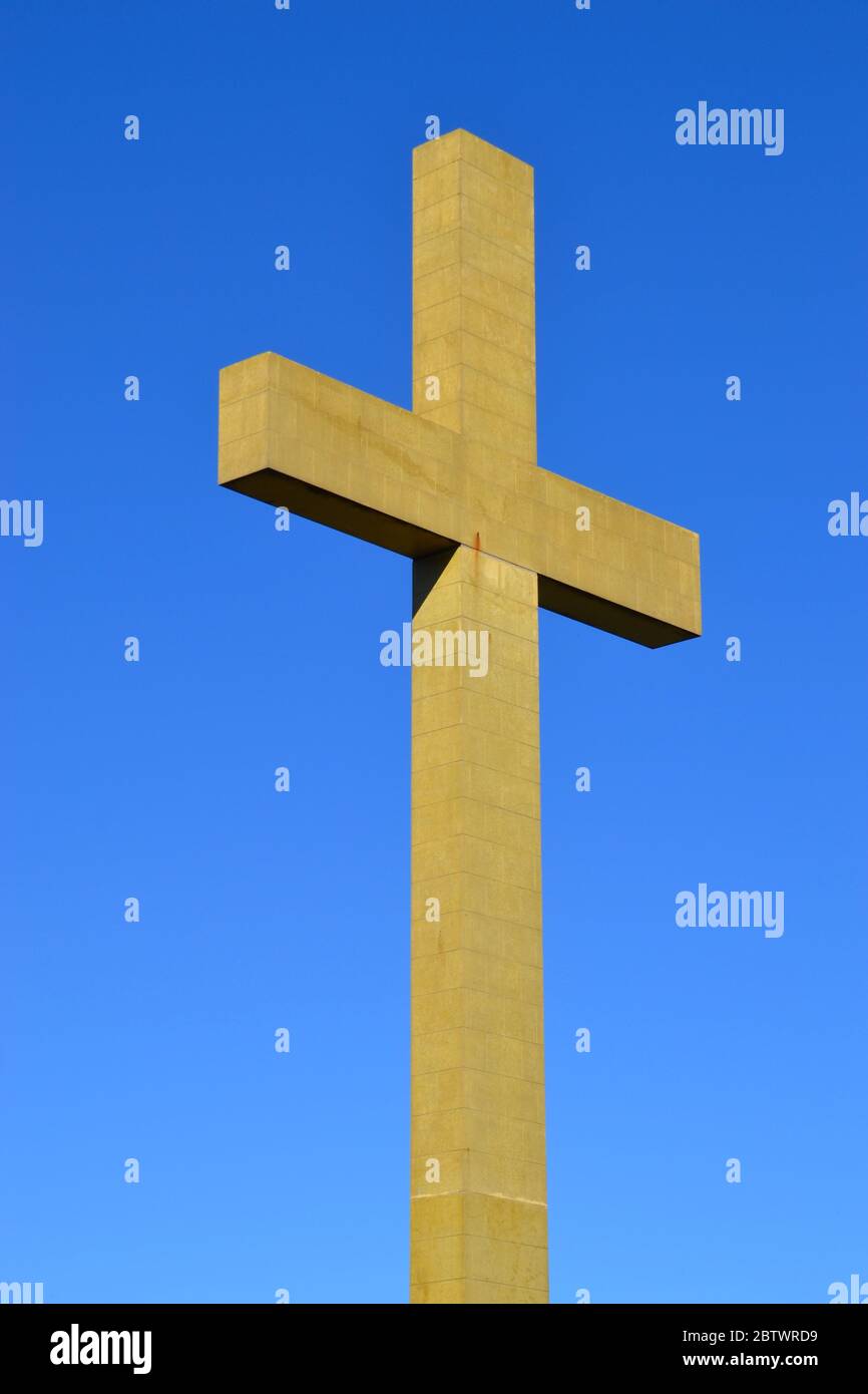 Upright concrete cross or crucifix in the sun against a clear blue sky ...
