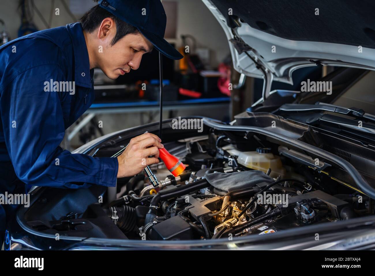 male mechanic holding and shining flashlight to checking a car engine ...