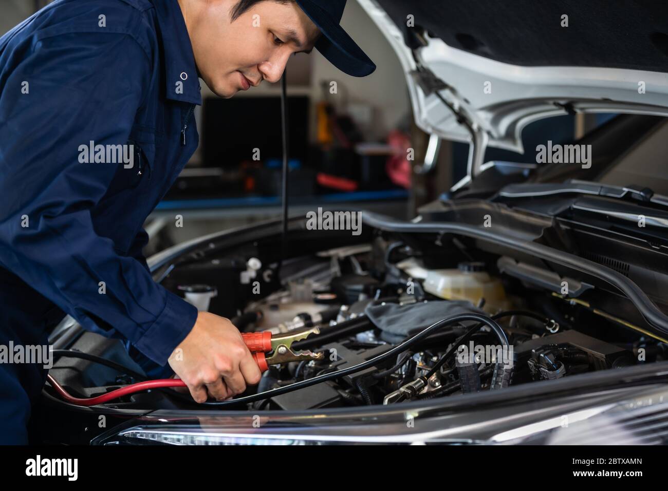 male mechanic charging battery of a car with electricity through jumper ...