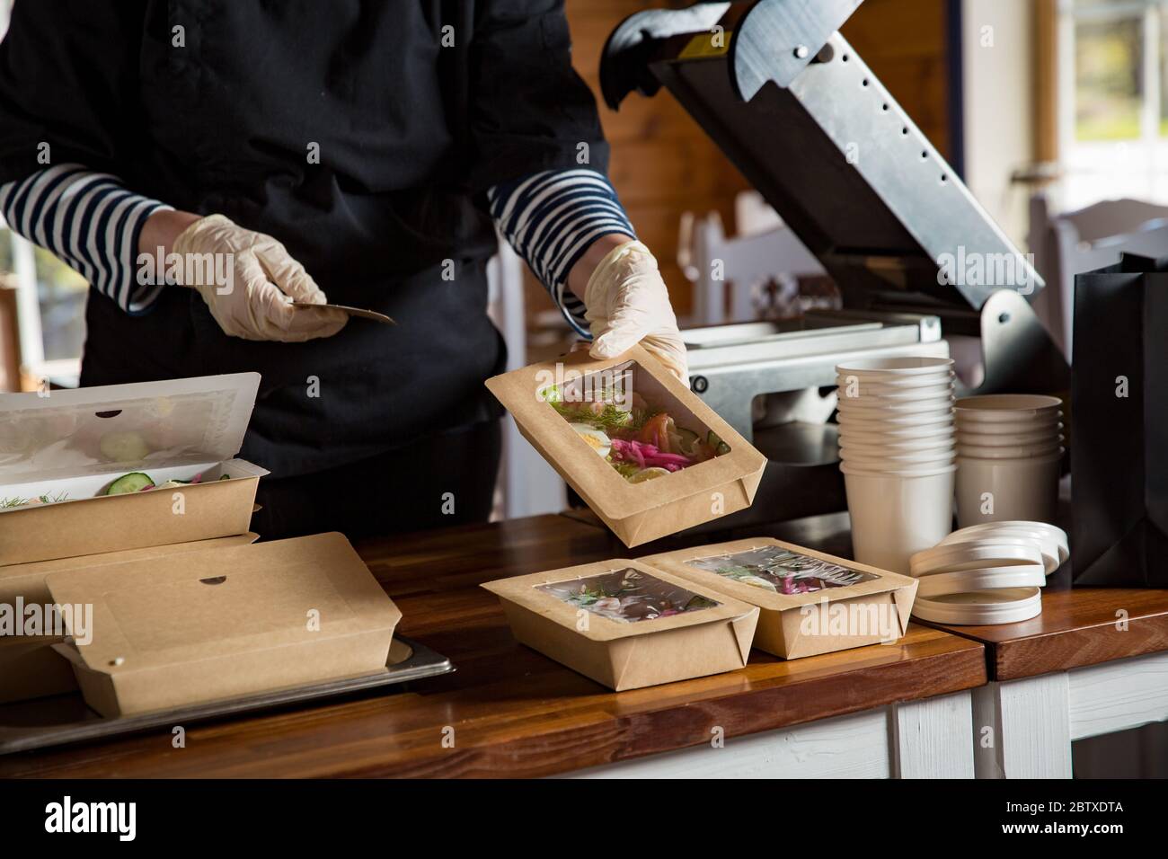Restaurant worker wearing protective mask and gloves packing food boxed ...