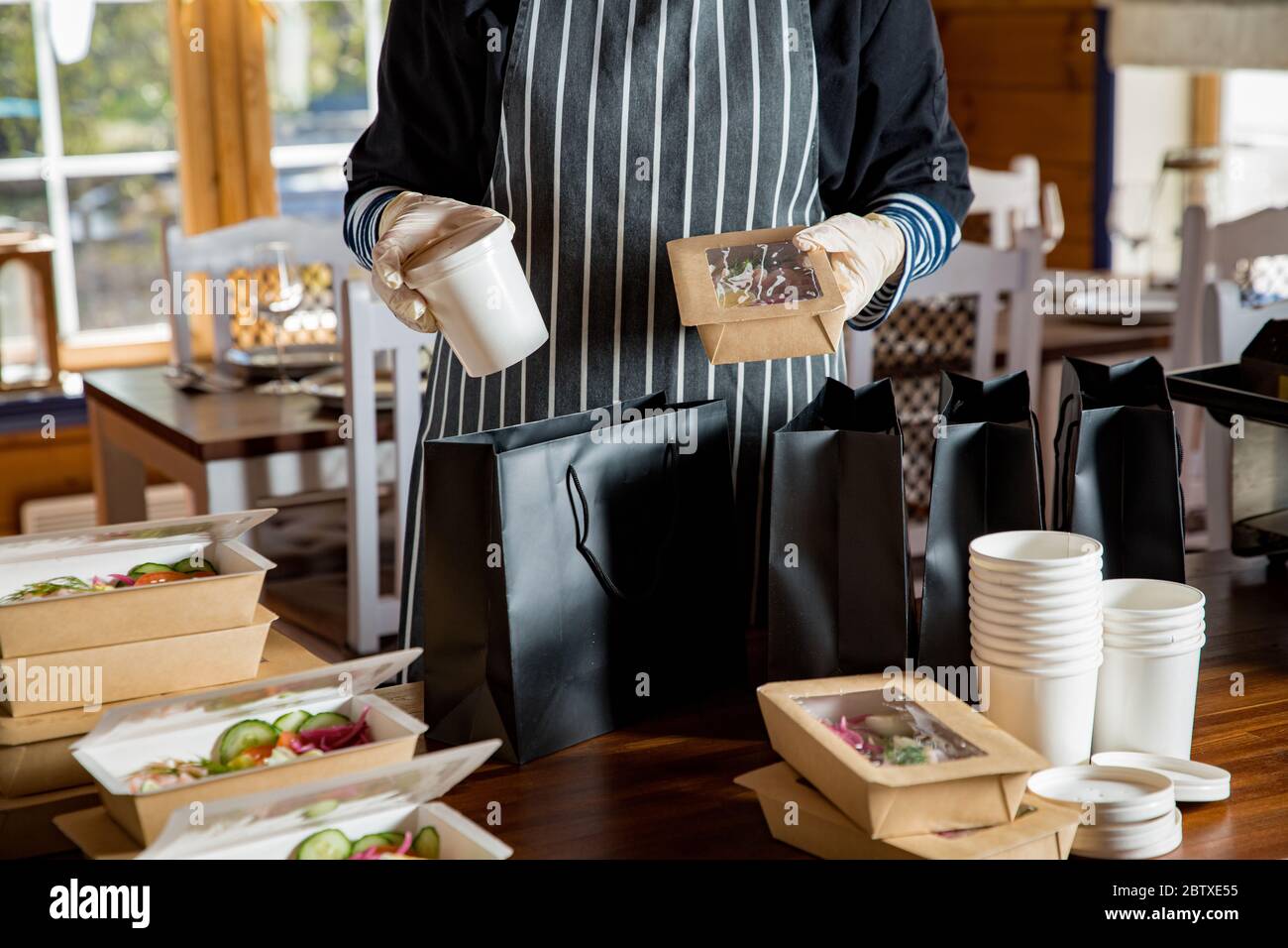 Restaurant worker wearing protective mask and gloves packing food boxed ...