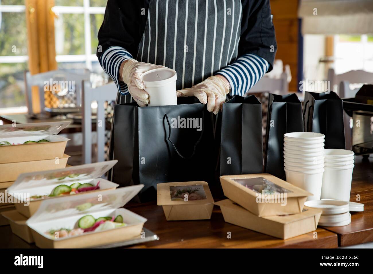 Restaurant worker wearing protective mask and gloves packing food boxed ...
