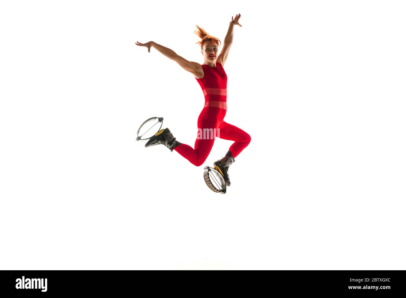 Beautiful redhead woman in a red sportswear jumping in a kangoo jumps ...