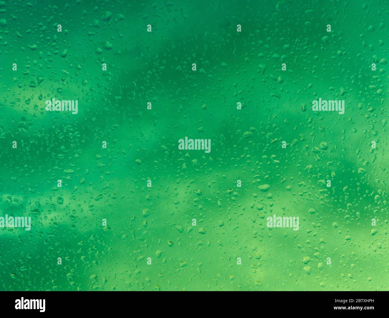 Wet green window with rain drops and a cloudy sky outside background ...