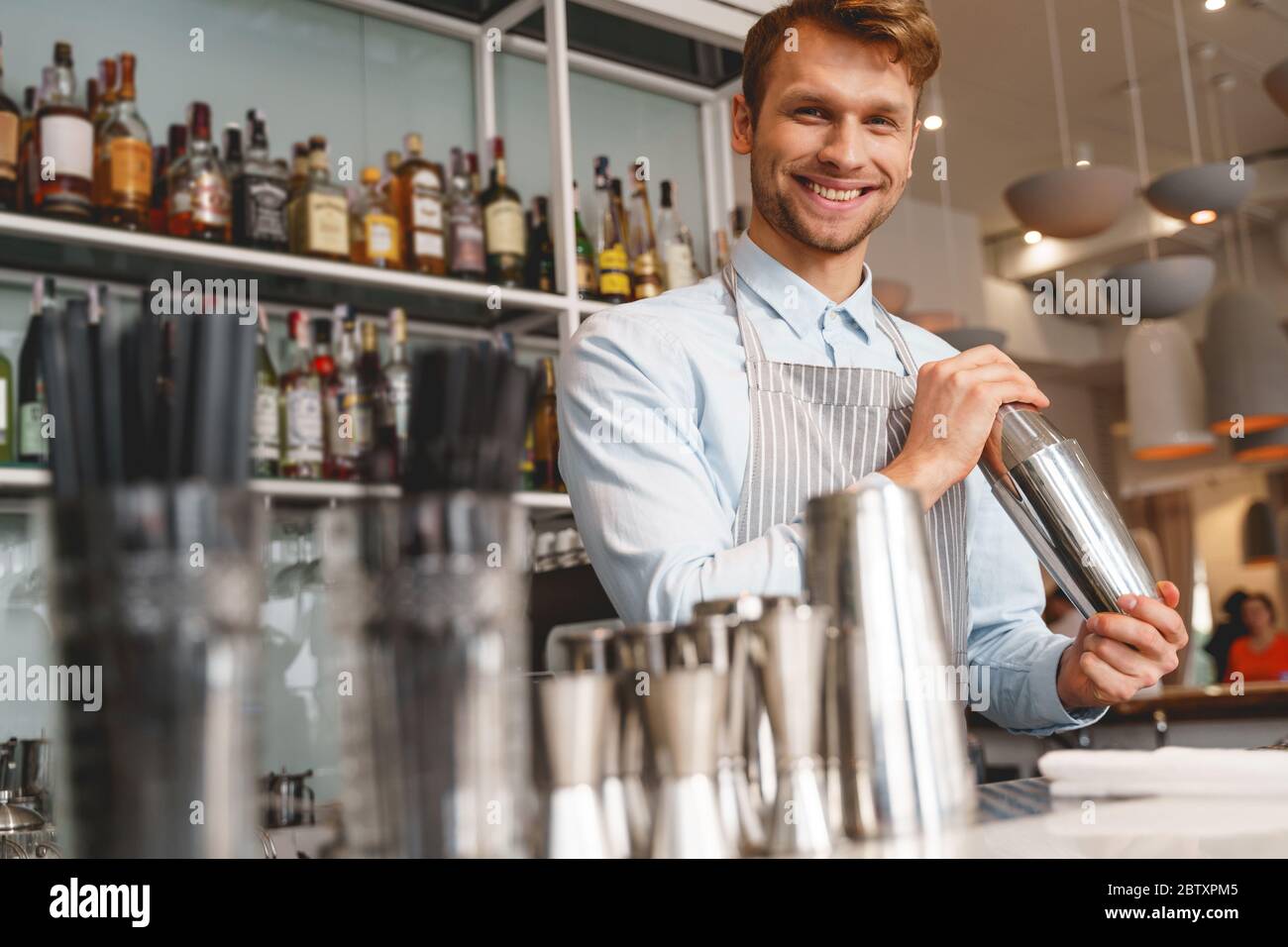 Cheerful bartender in apron mixing cocktail with shaker Stock Photo - Alamy