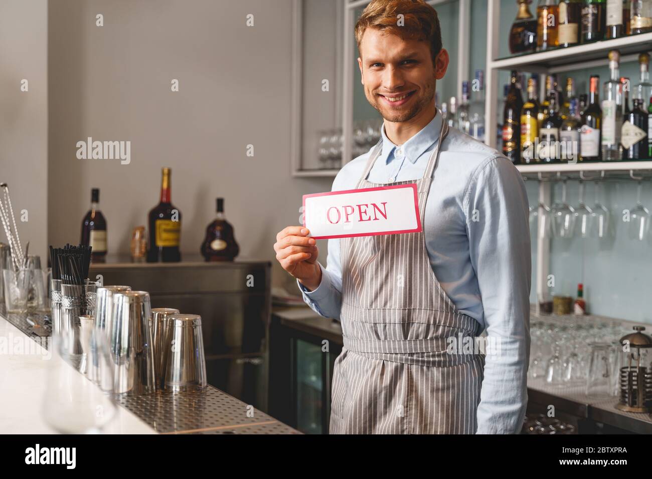 Cheerful bartender in apron holding open sign Stock Photo - Alamy