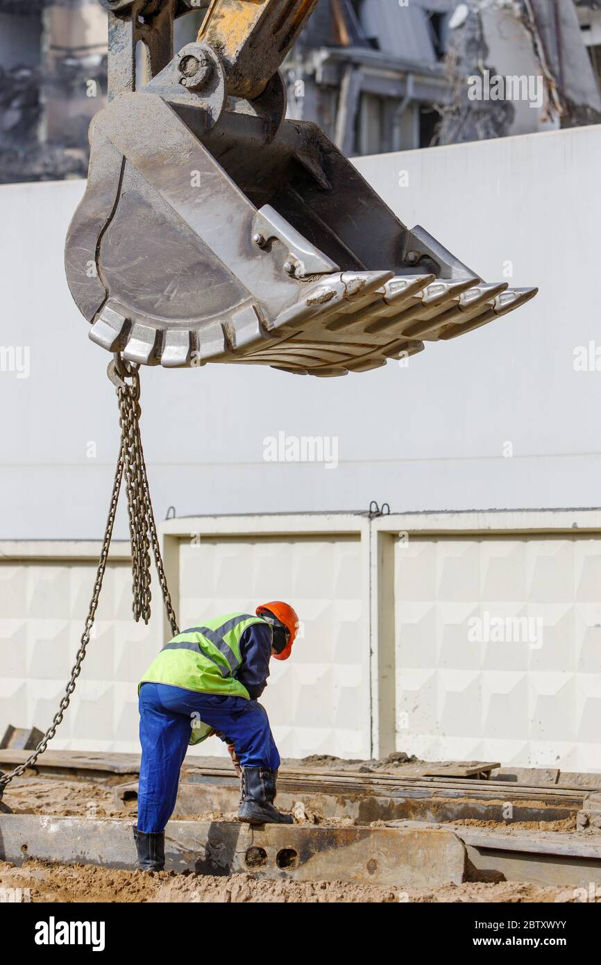 Excavator bucket lifting metal beam with worker helping, construction ...