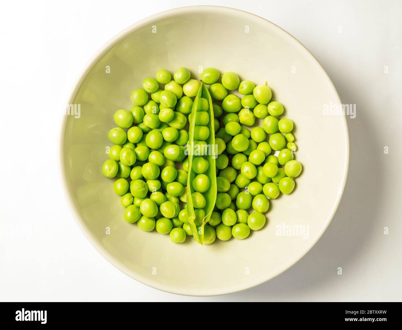 A bowl of freshly shelled peas with a single pod full of peas from ...
