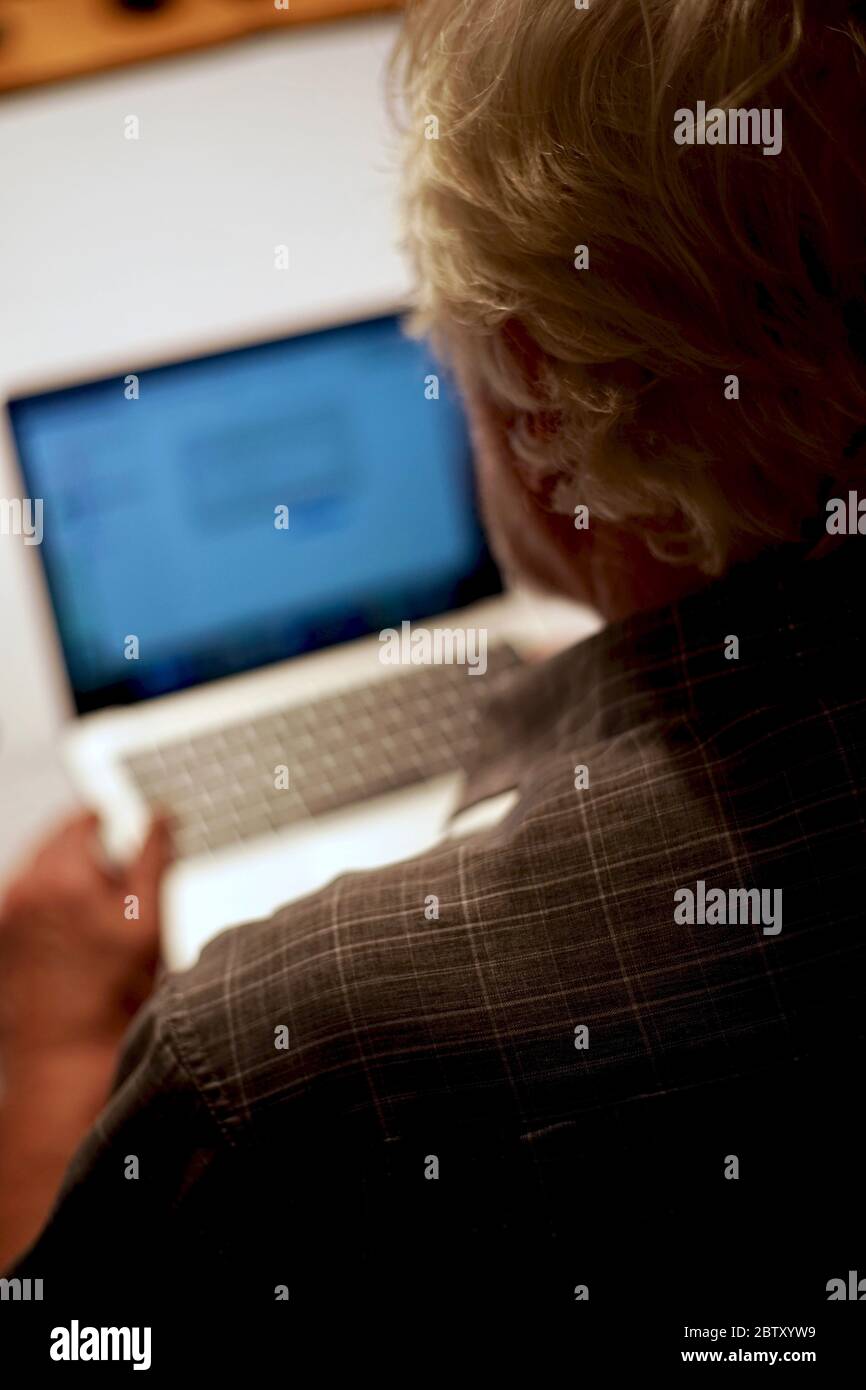 Over shoulder back view of white haired retired senior man using laptop ...