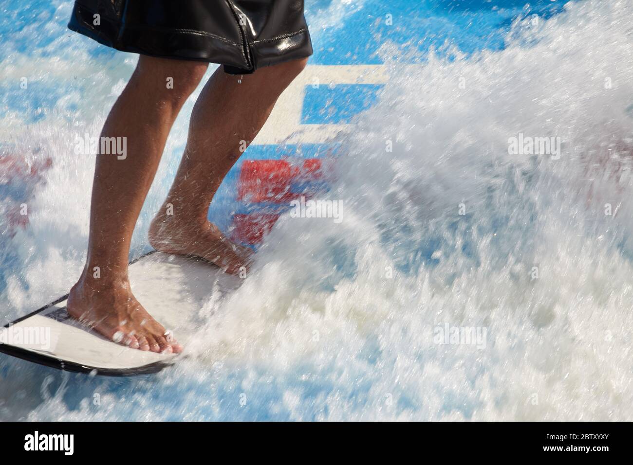 Man riding a surfboard or foot board along an outdoor water slide set ...