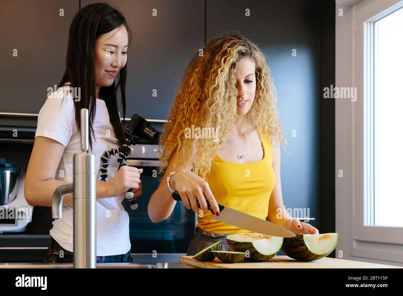 Blonde woman with curly hair cutting a melon while an asian woman is ...