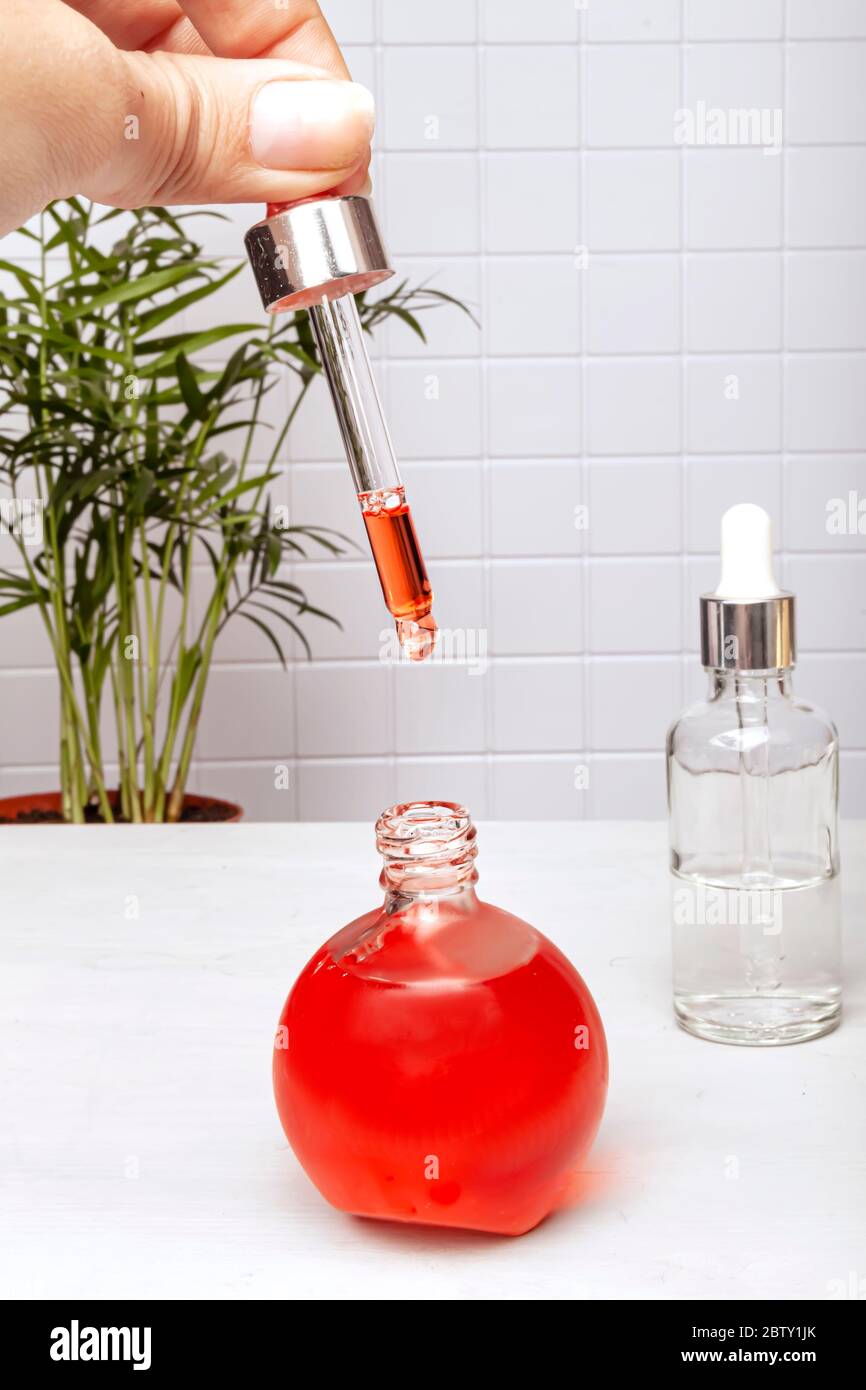 Hand holds medical dropper with liquid and a drop falling over a bottle ...