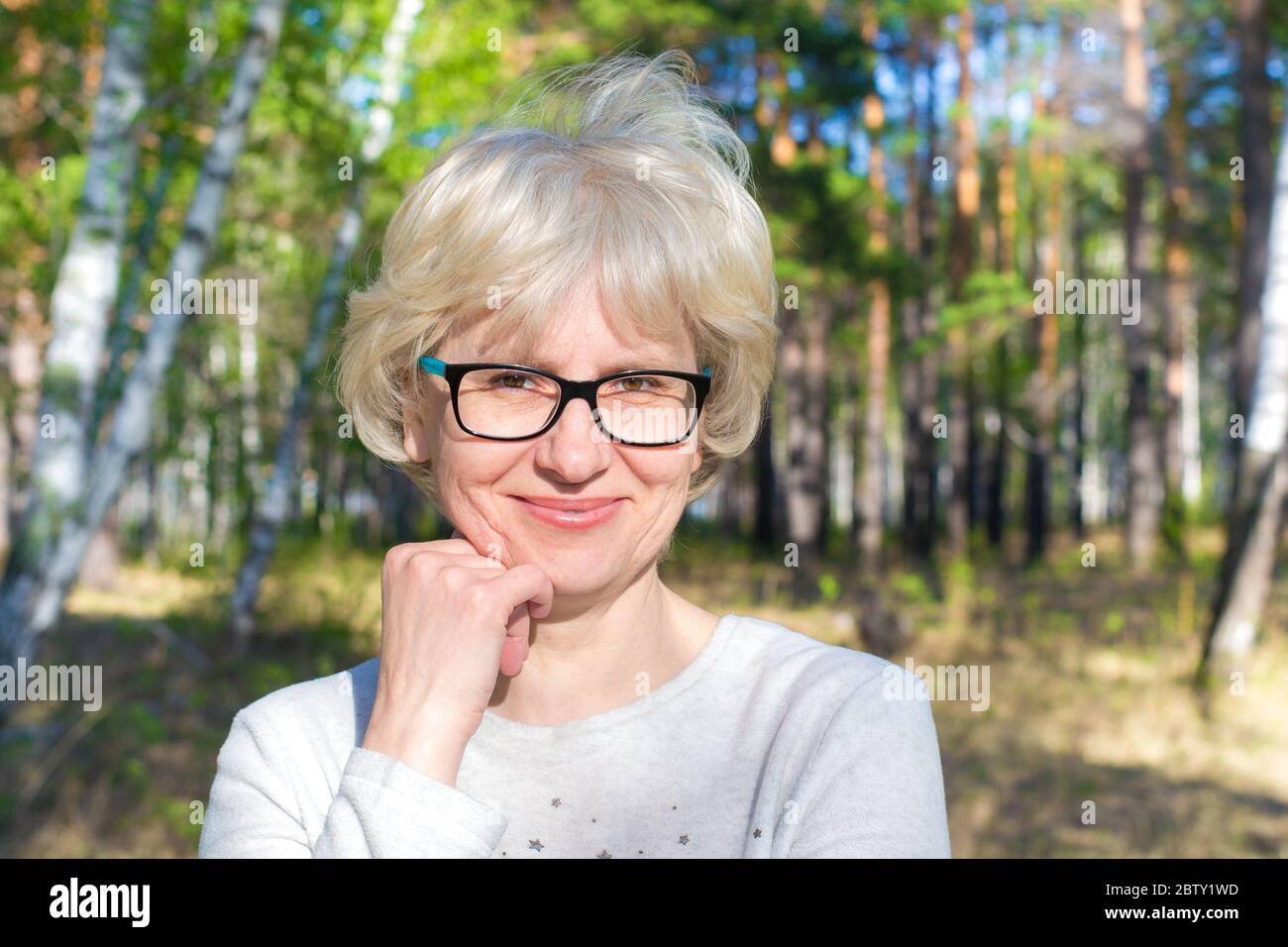Portrait of a happy middle-aged woman with glasses walking in the park ...