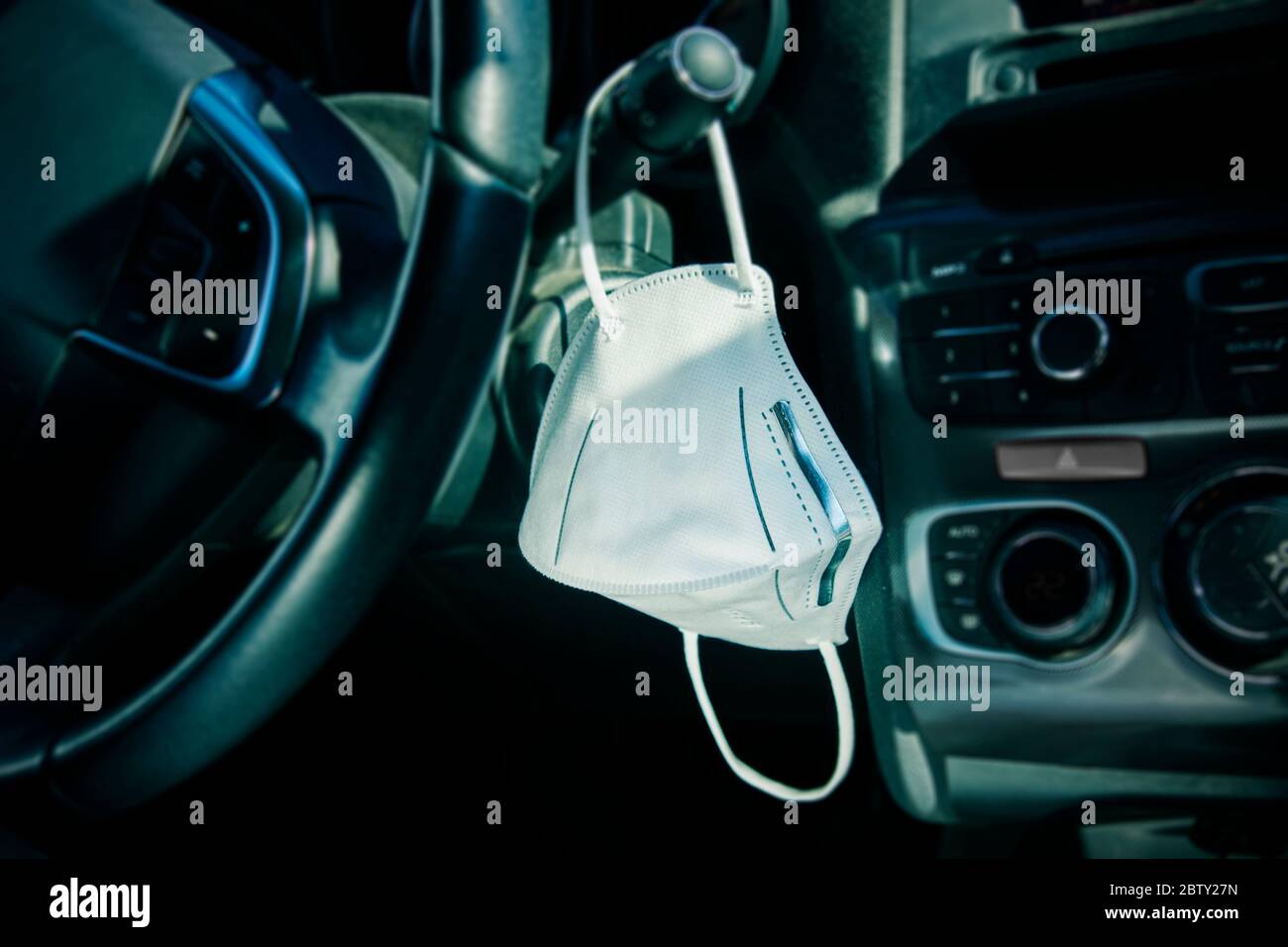 closeup of a face mask hanging from a lever on the dashboard of a car ...