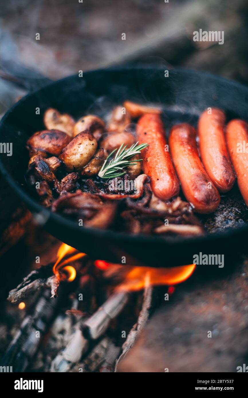 Fried mushrooms and bacon with sausages in a pan in the woods on fire ...