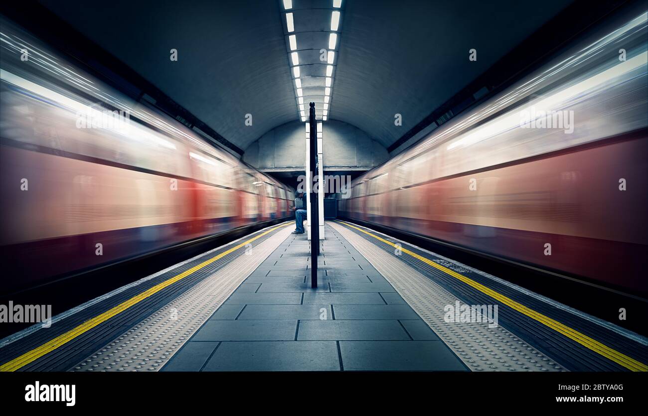 Two trains in motion and a seated commuter at London Tube Station ...