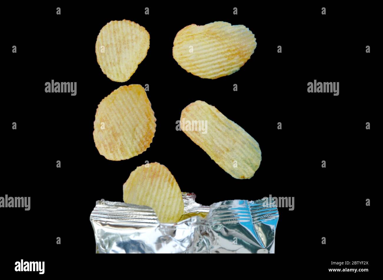 potato chip falling to aluminium foil packaging on black background ...