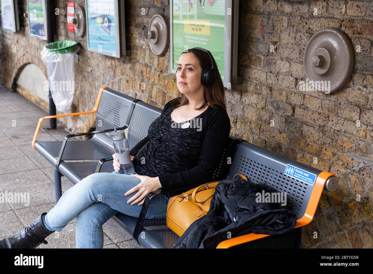 Pregnant women wearing a "baby on board" badge sitting on bench at ...