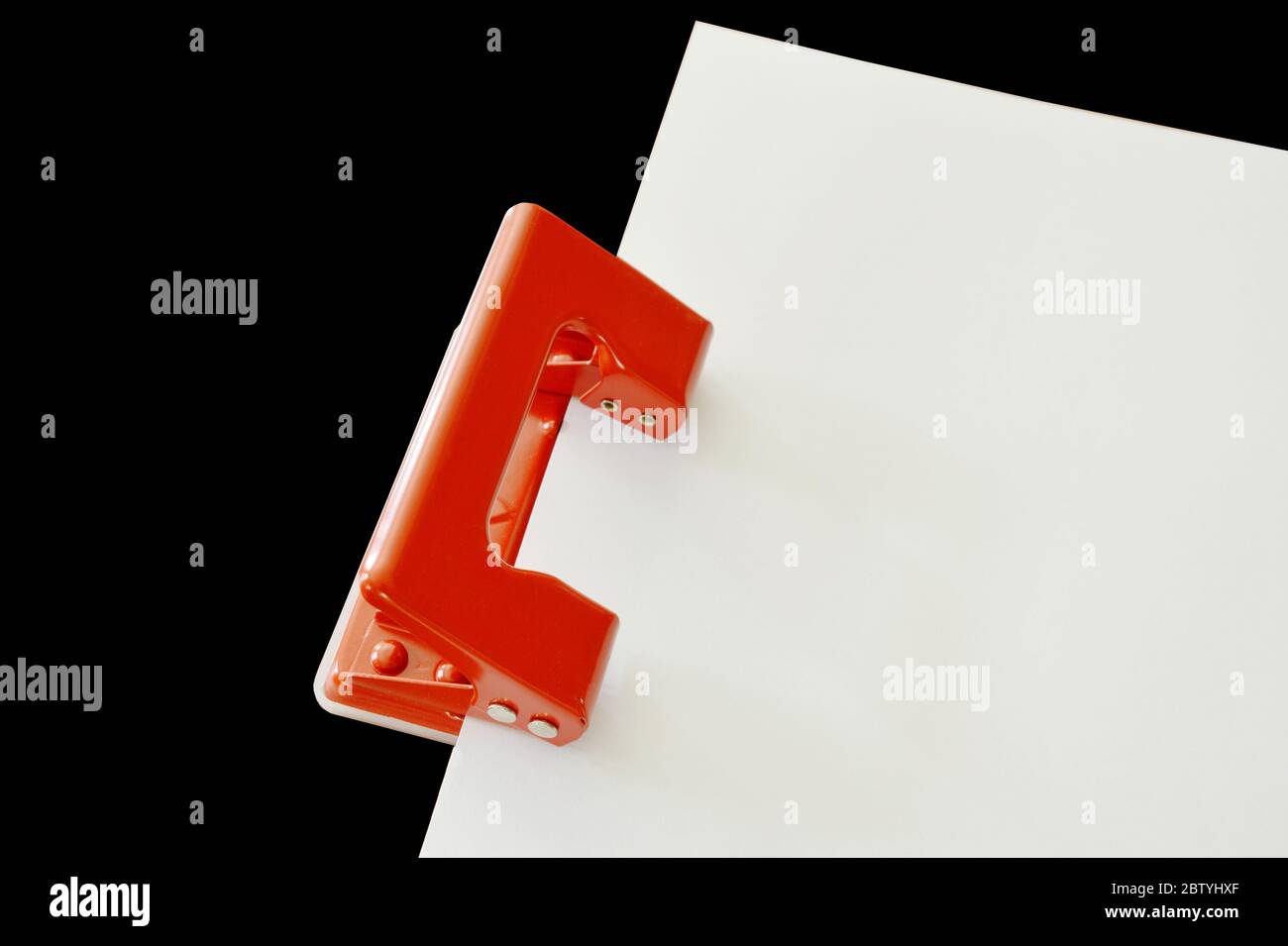 red punch pushing on white paper in black background Stock Photo - Alamy