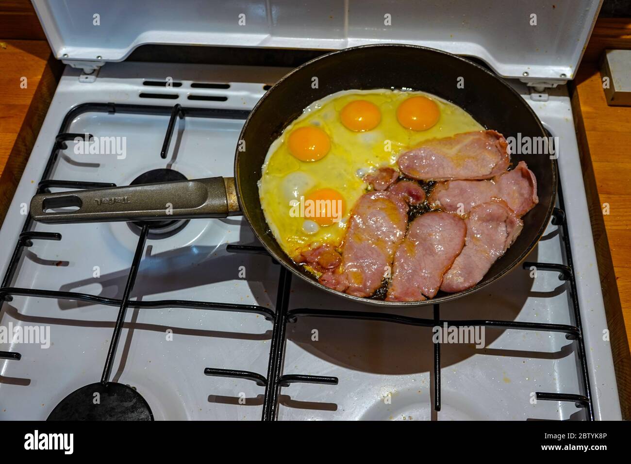 English breakfast, a frying pan on gas cooker with bacon and eggs ...