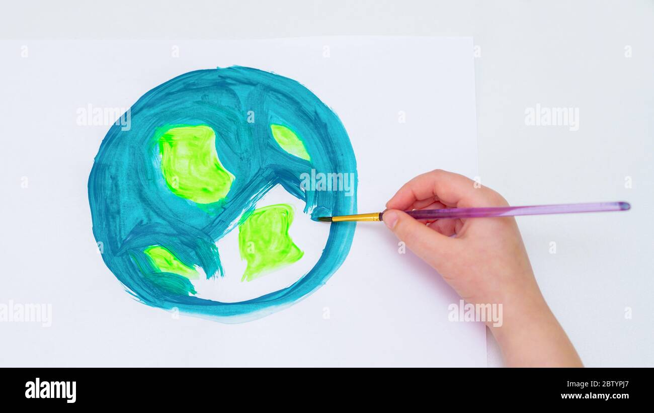 Top view of little girl is drawing earth by watercolors on white paper ...