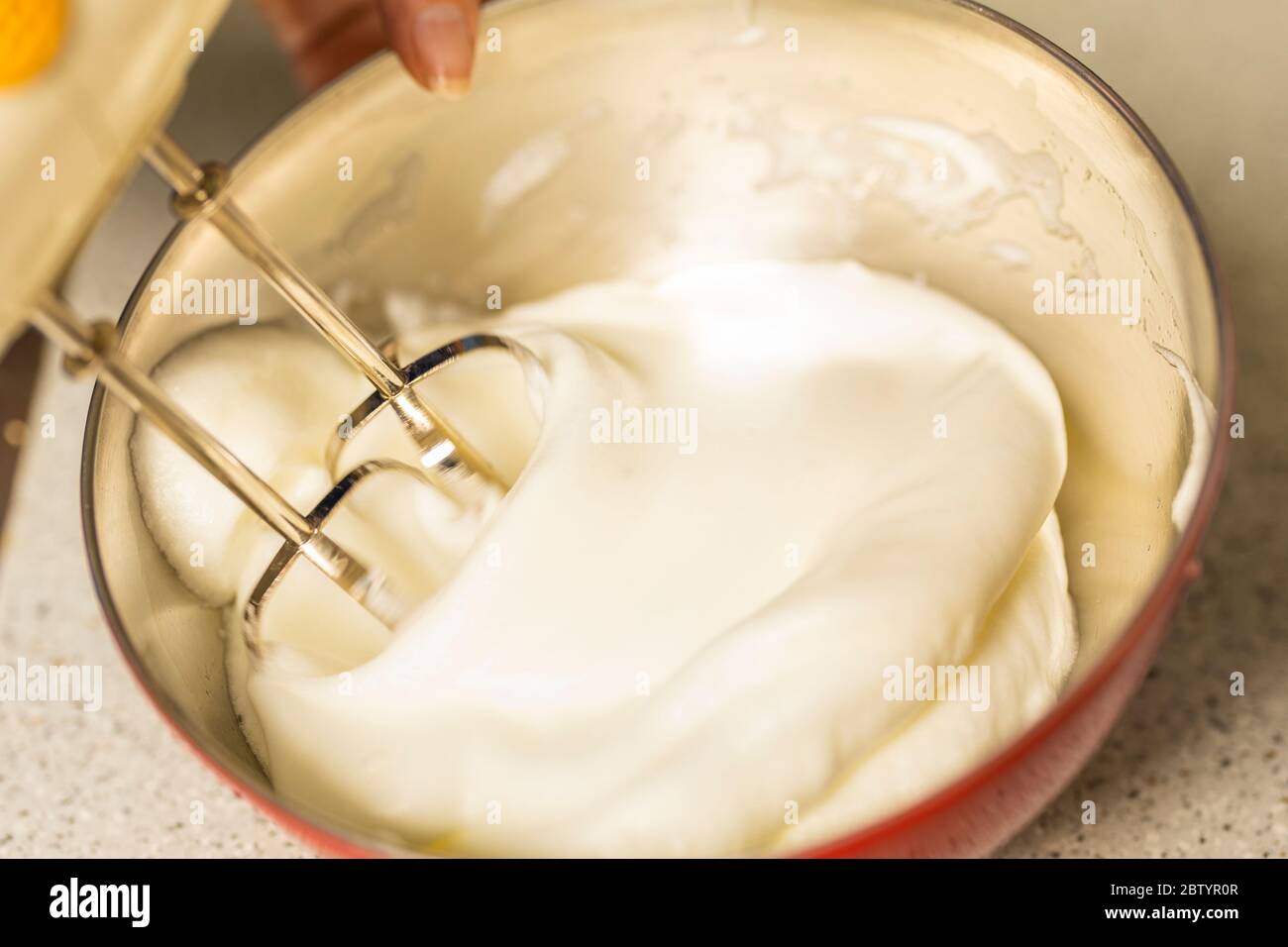 Beating a white cream with a mixer in a metal bowl. Whipped cream ...