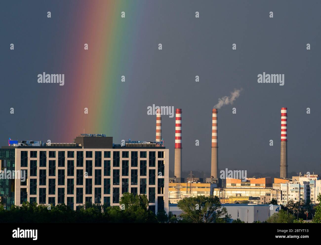 Power plant chimneys and bright rainbow against dark sky after storm ...