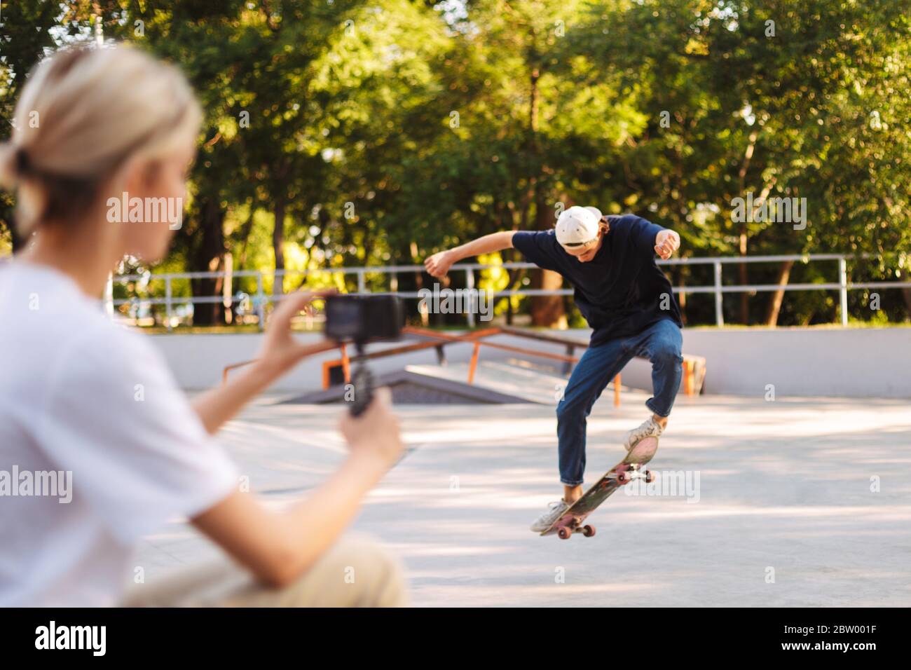 Young skater practicing stunts on skateboard while pretty girl ...