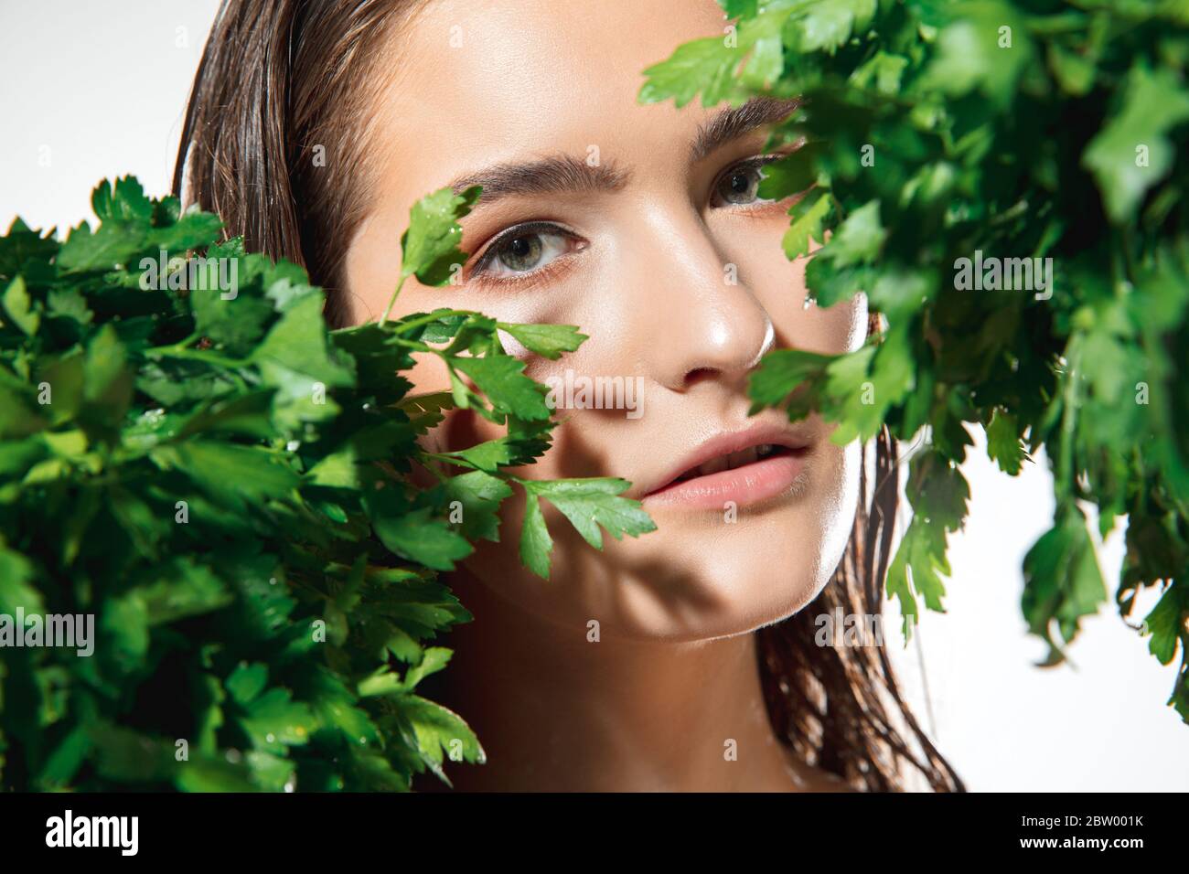 Close up of beautiful female face with green fresh parsley on white ...