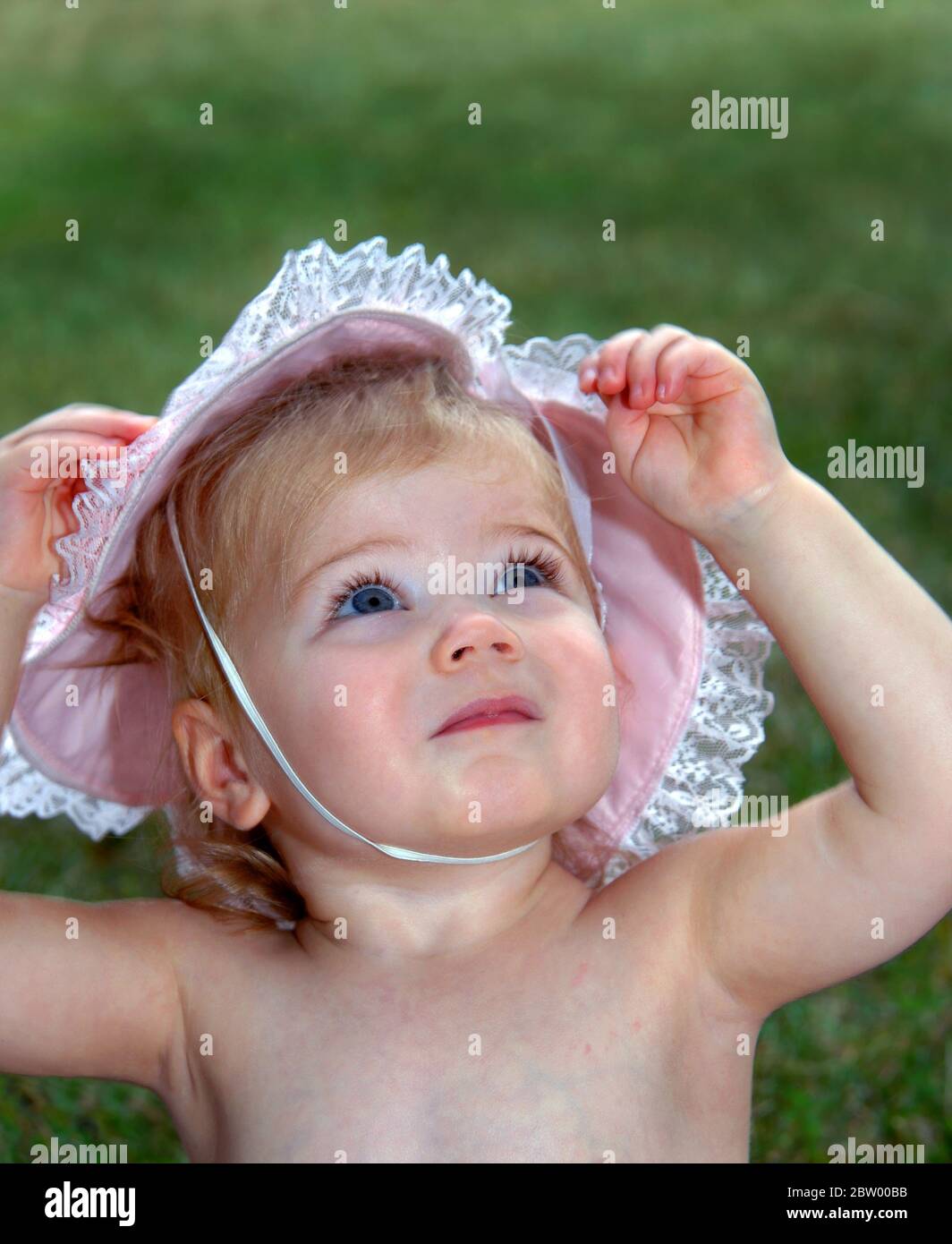 Little girl models a pink and white frilly hat. She is touch hat with ...