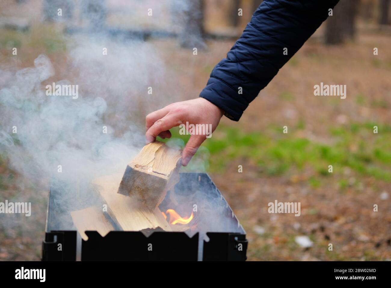 Grilling season in nature open. Man's hand is adding wood into the fire ...