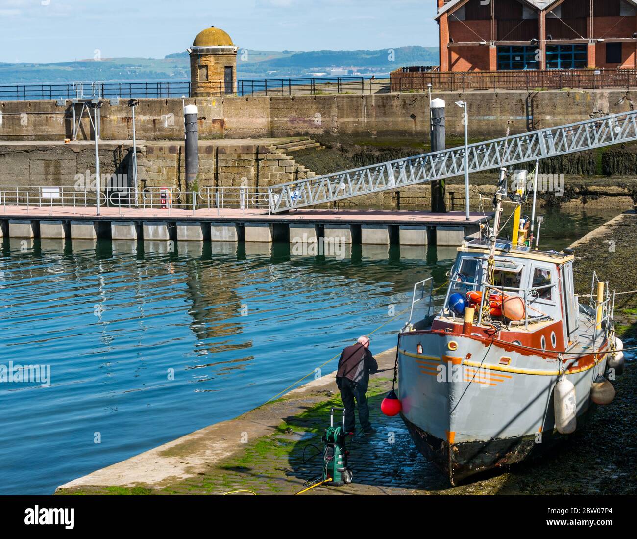 Man cleaning hull of fishing boat with jet hose, Newhaven Harbour ...