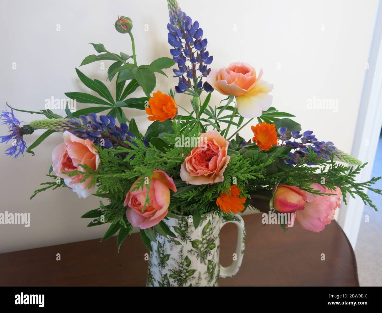 An arrangement of summer cut flowers in a jug, featuring purple lupins ...