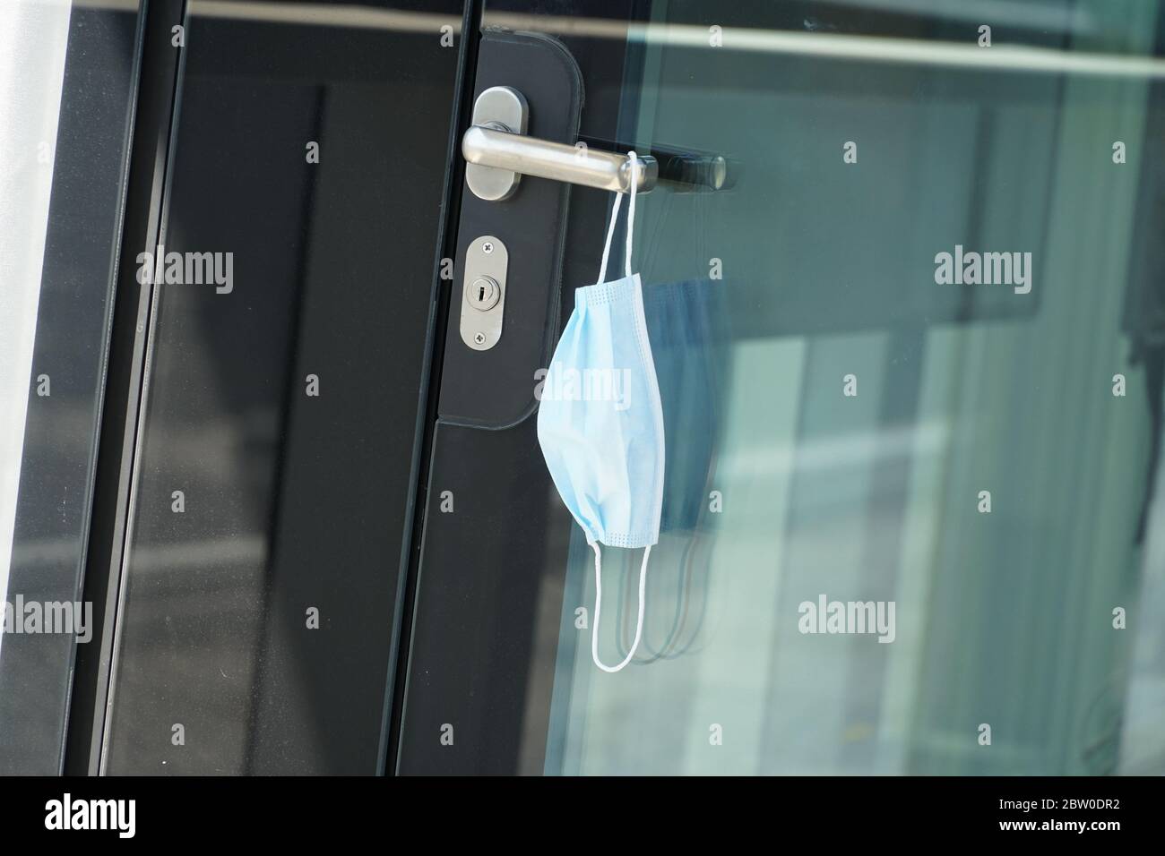 A face mask suspended on a door handle in a corporate building, close ...