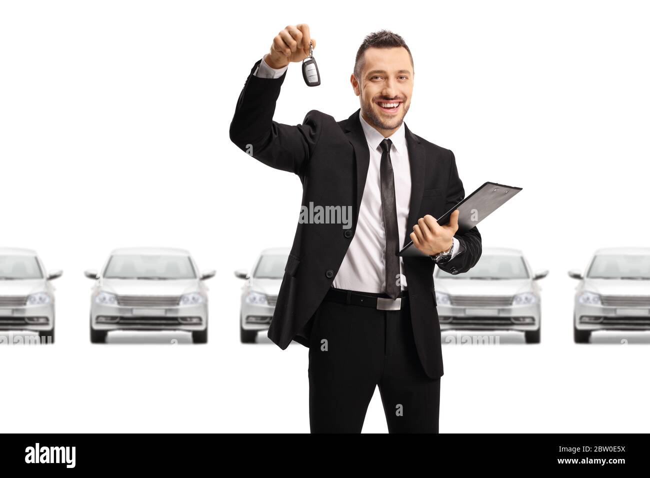 Car dealer holding a car key and documents in front of silver cars ...