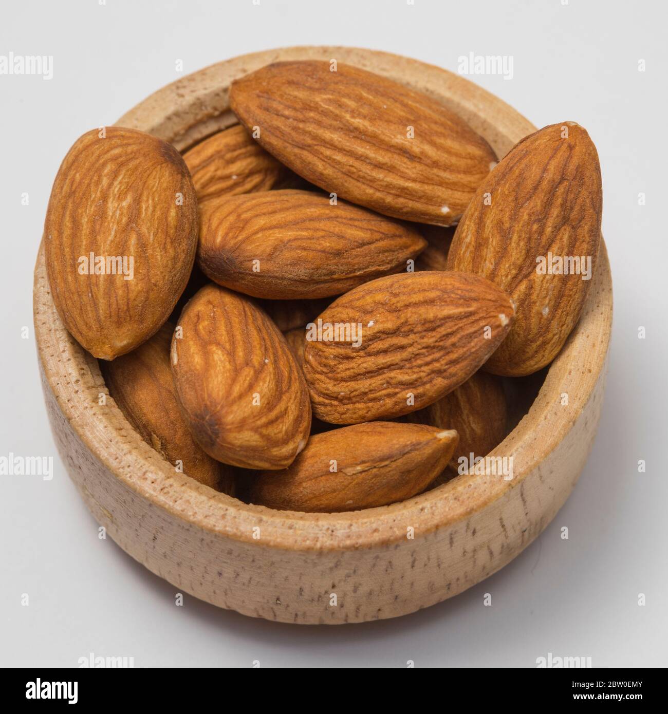 Close-up view of almonds in a small wooden bowl on white background ...