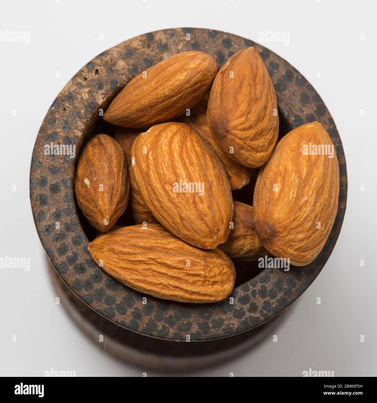 Close-up view of almonds in a small wooden bowl on white background ...