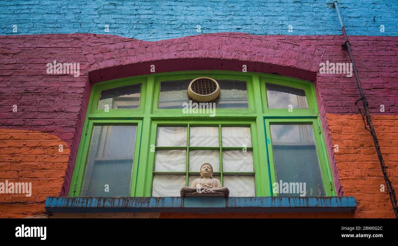 Colourful window frame with a Buddha statue against a coloured pained ...