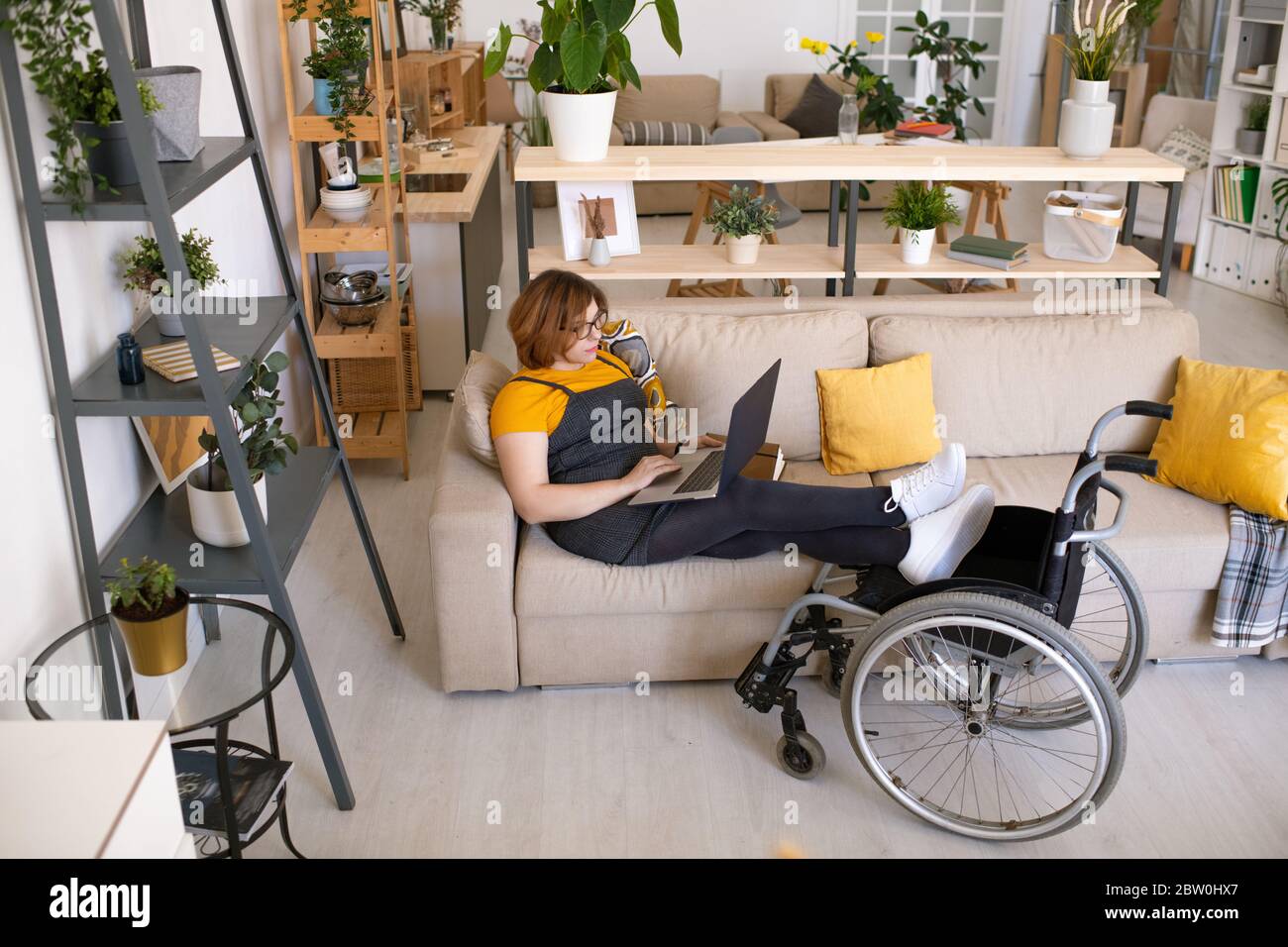 Busy young handicapped woman sitting with feet on wheelchair and using ...