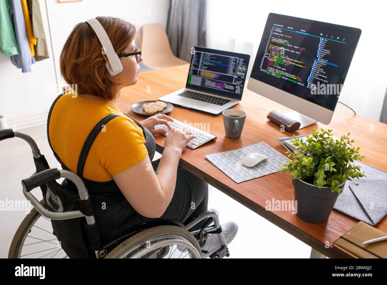 Female freelance programmer in modern headphones sitting in wheelchair ...