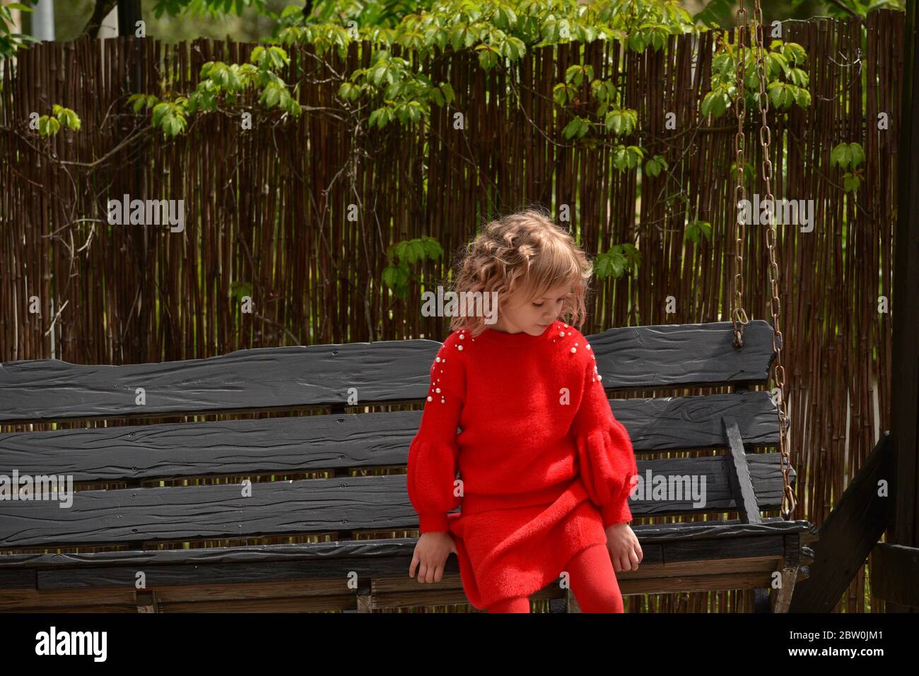 Girl 7 years old in red clothes on the street on a swing. Spring ...