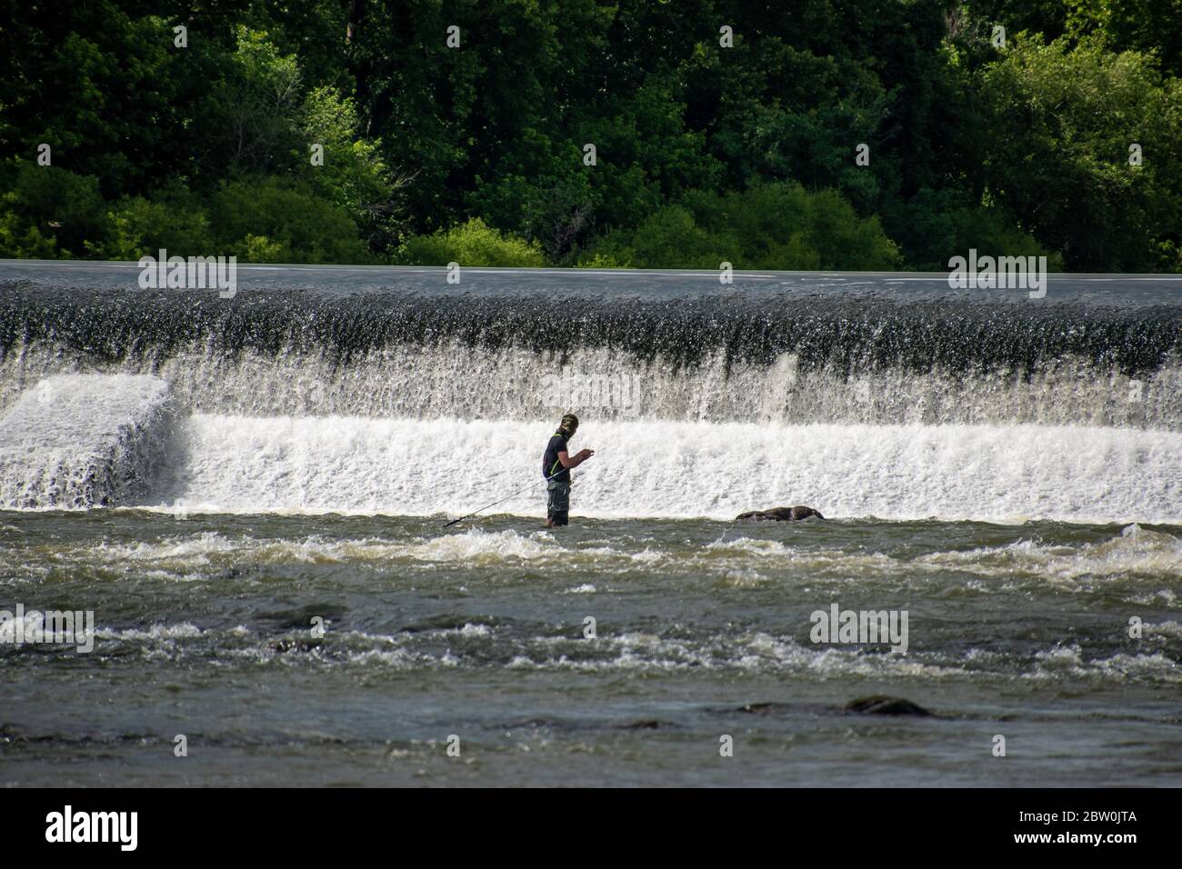 A single person fly fishing next to a waterfall caused by a dam on the ...