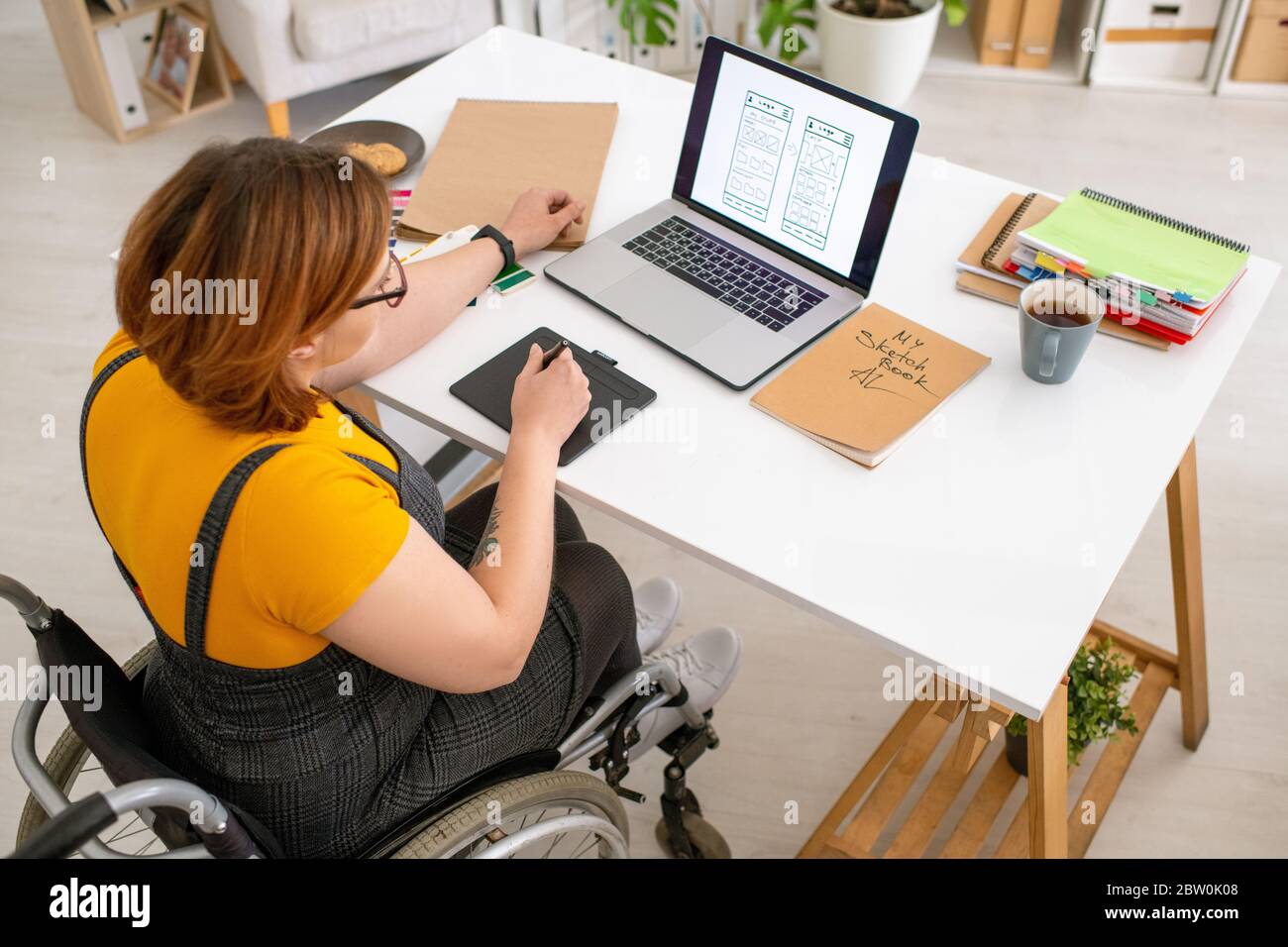 Disabled UI designer sitting in wheelchair and viewing sketch on laptop ...