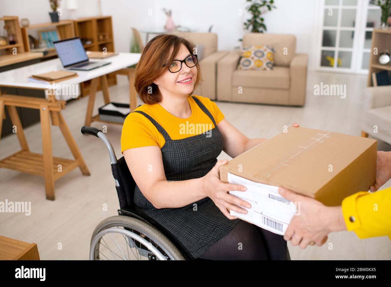 Unrecognizable deliveryman giving package to satisfied disabled woman ...
