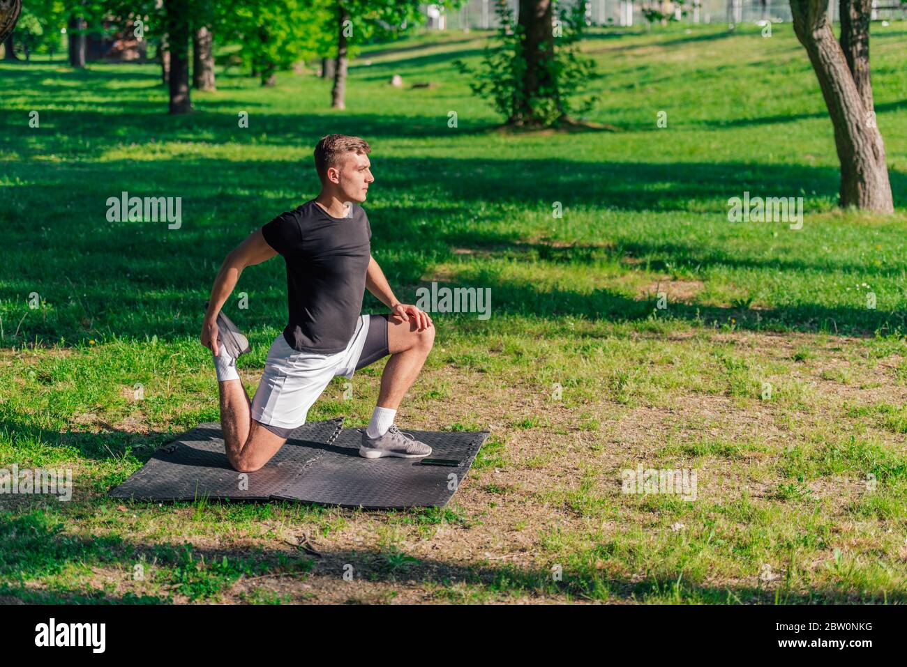 Sporty young man stretching legs and doing forward lunge while having ...