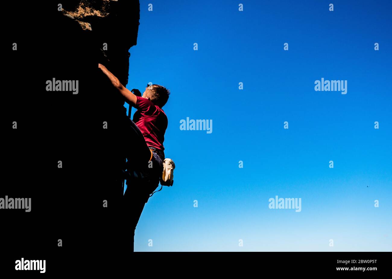 Man reaching for a grip while he rock climbs on a steep cliff Stock ...
