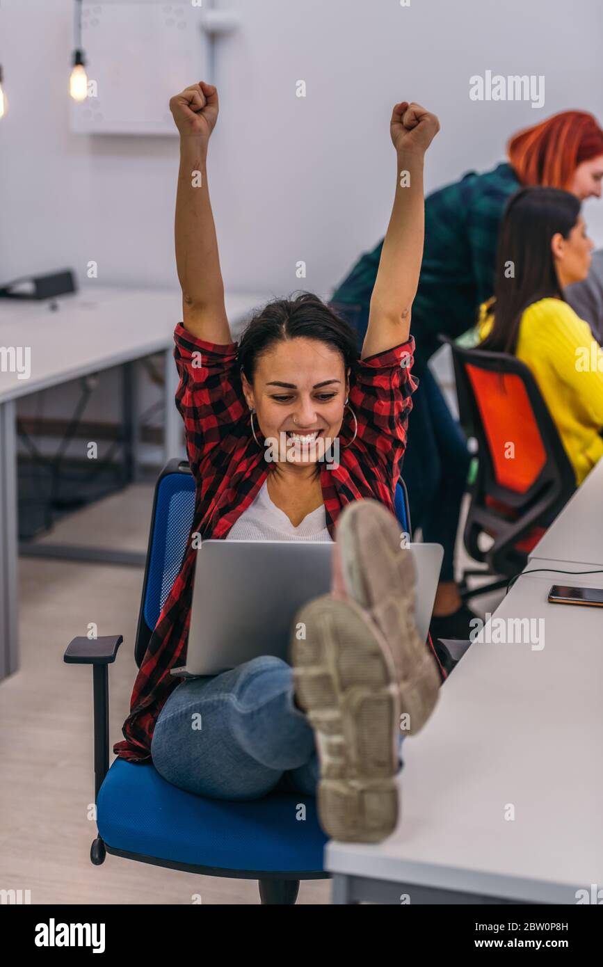 A young female worker with her hands up in the air, her legs on the ...